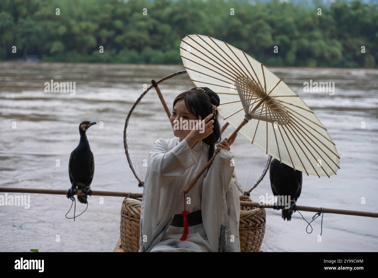 Hanfu girl fixing her hair and holding parasol while standing on bamboo ...