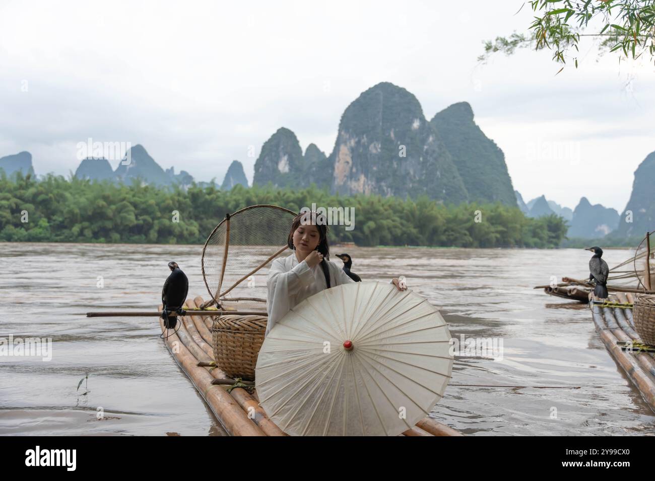 Barefoot girl in Hanfu clothing stands with an umbrella on a bamboo ...