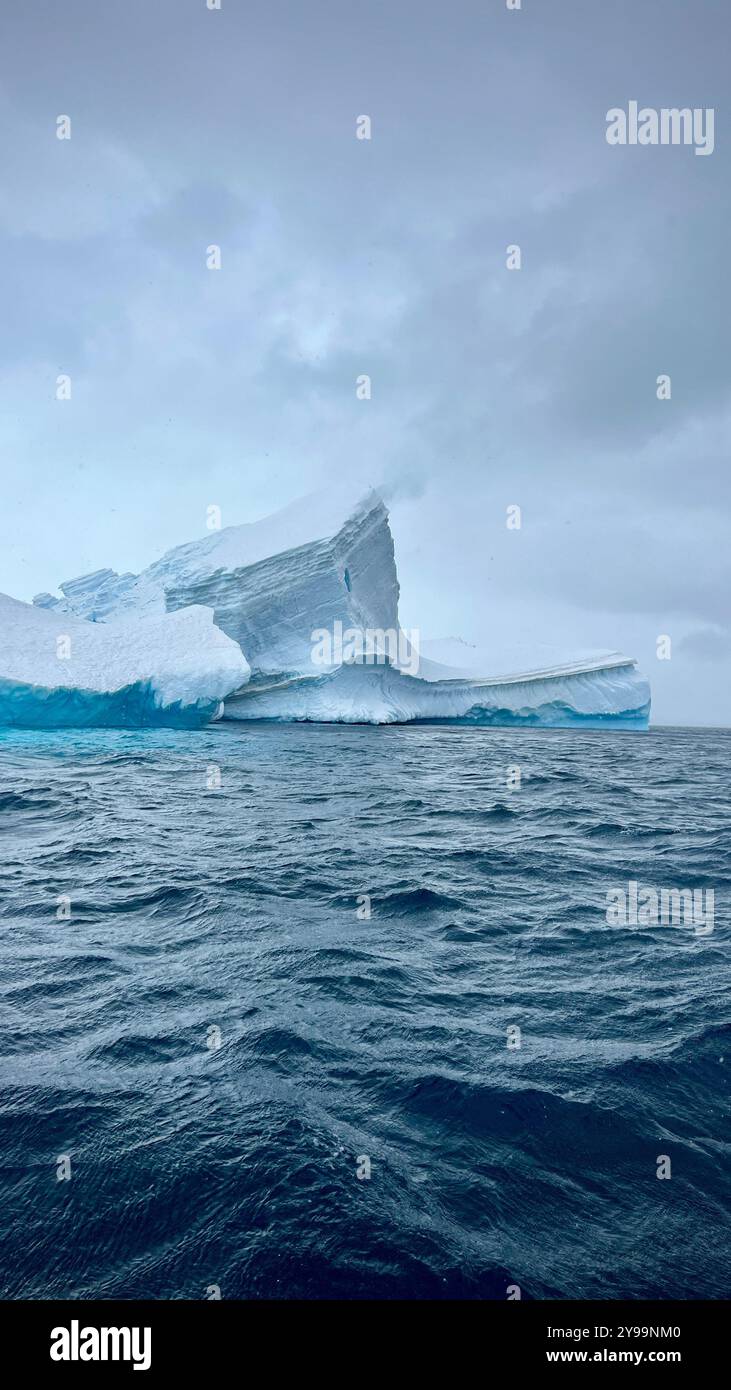 A massive jagged iceberg floats in the dark, choppy waters of the ...