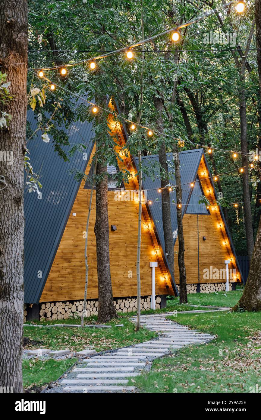 Modern A-frame cabins with glowing string lights in forest environment ...