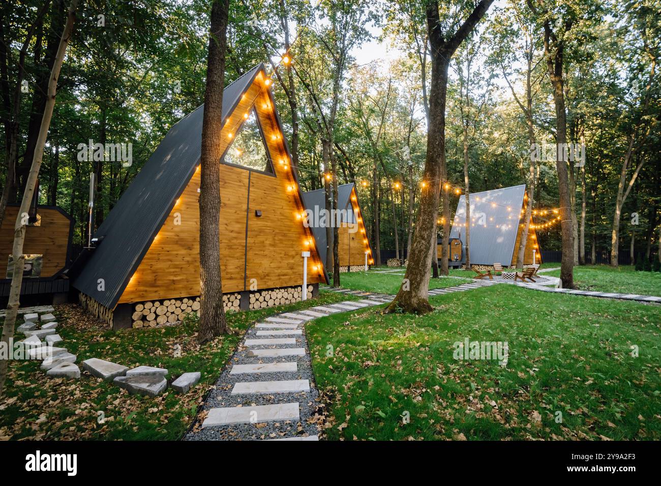 Cozy wooden A-frame cabins in forest with sunlight and outdoor seating ...