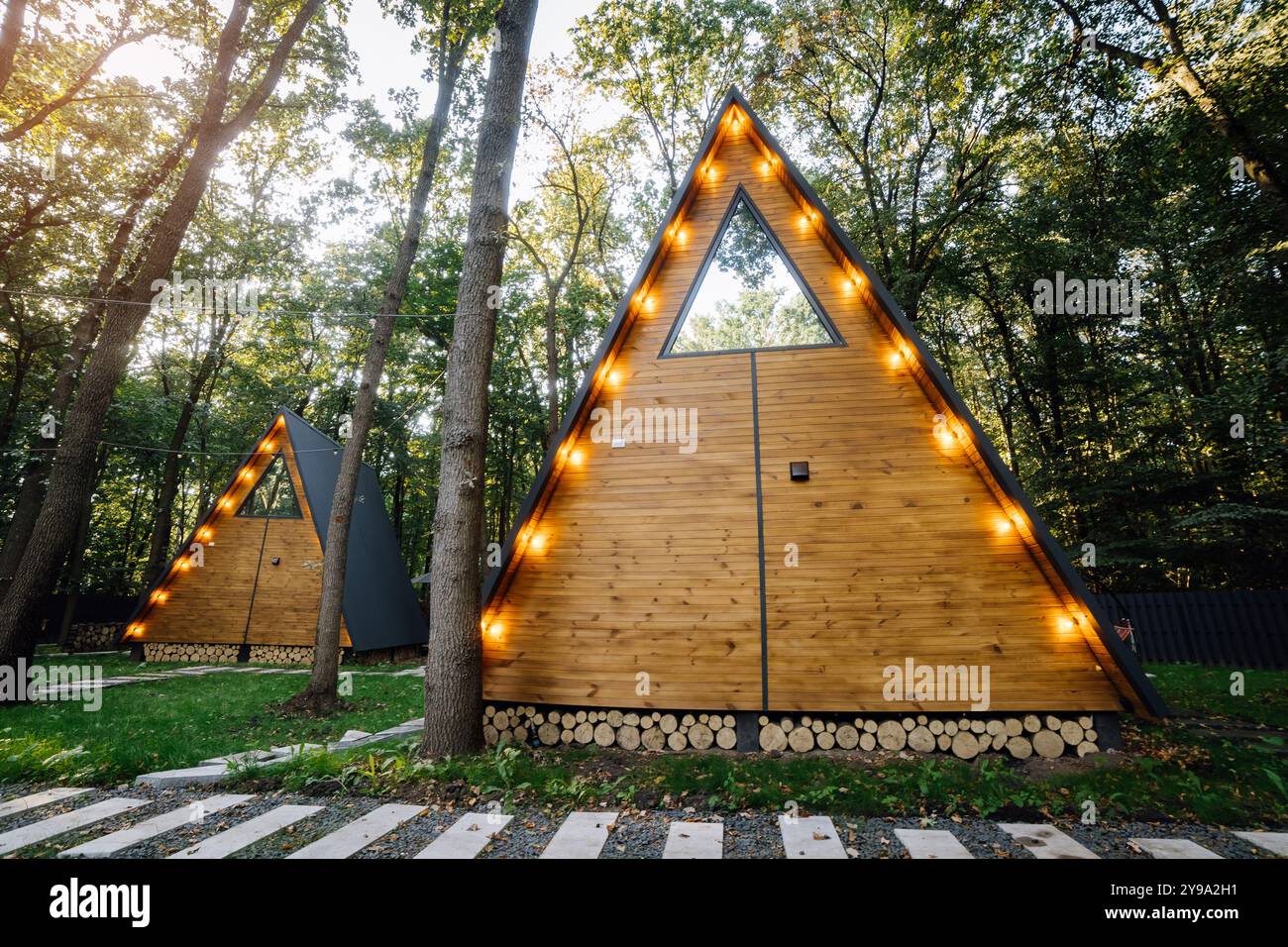 Cozy wooden A-frame cabins in forest with sunlight and outdoor seating ...