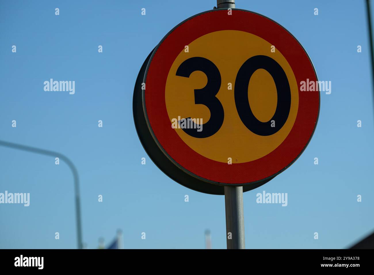 A bright yellow speed limit sign displaying 30 km/h stands tall against a clear blue sky ...