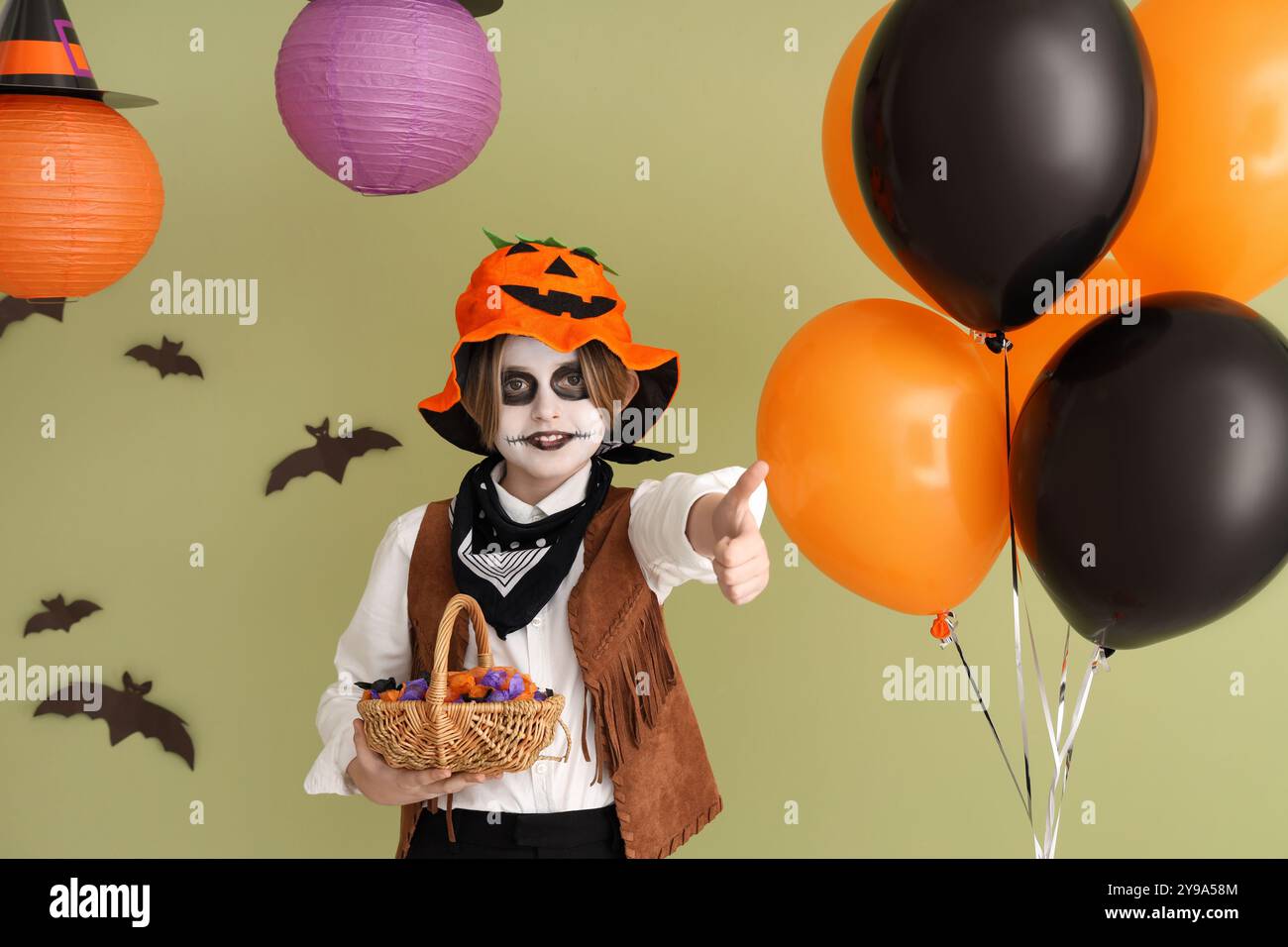 Little boy dressed for Halloween with candies and balloons near green ...