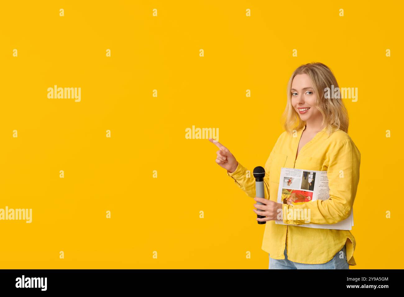 Portrait of female journalist with microphone and newspaper pointing at ...