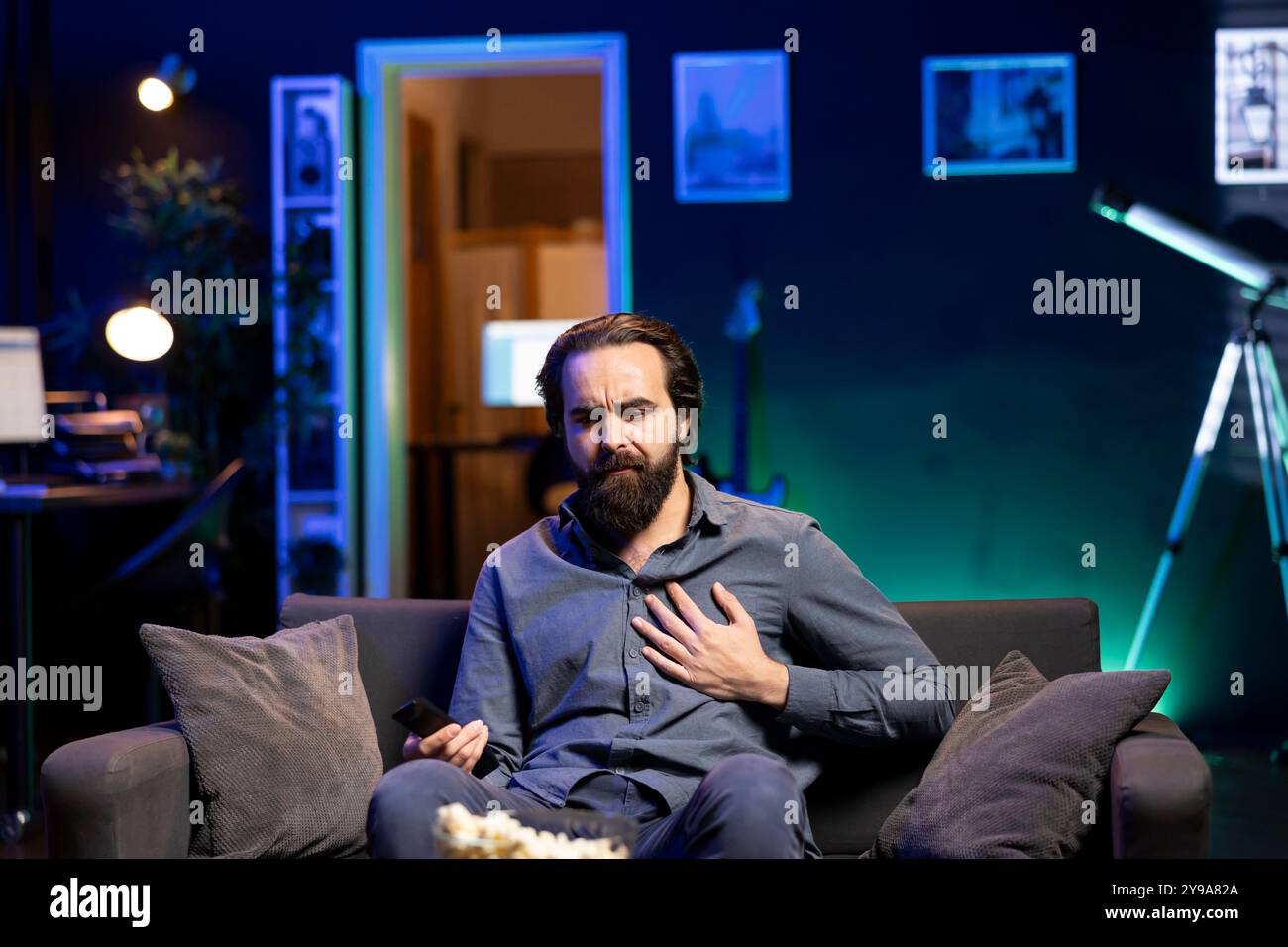 Man at home feeling discomfort in chest while watching TV on couch ...