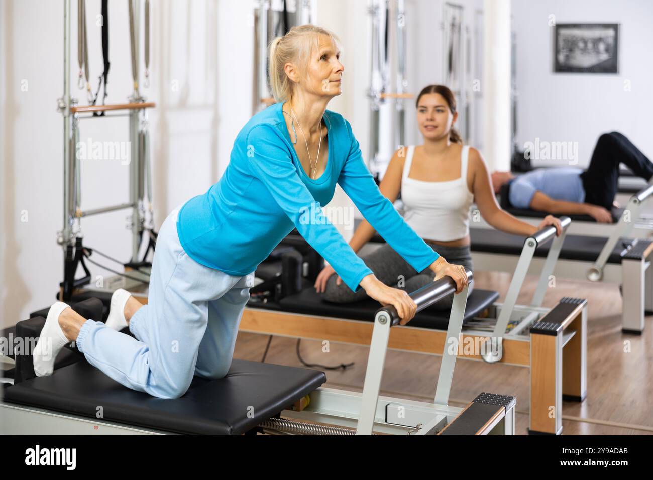 Mature female lying down on bed of Pilates reformer bed machine with ...