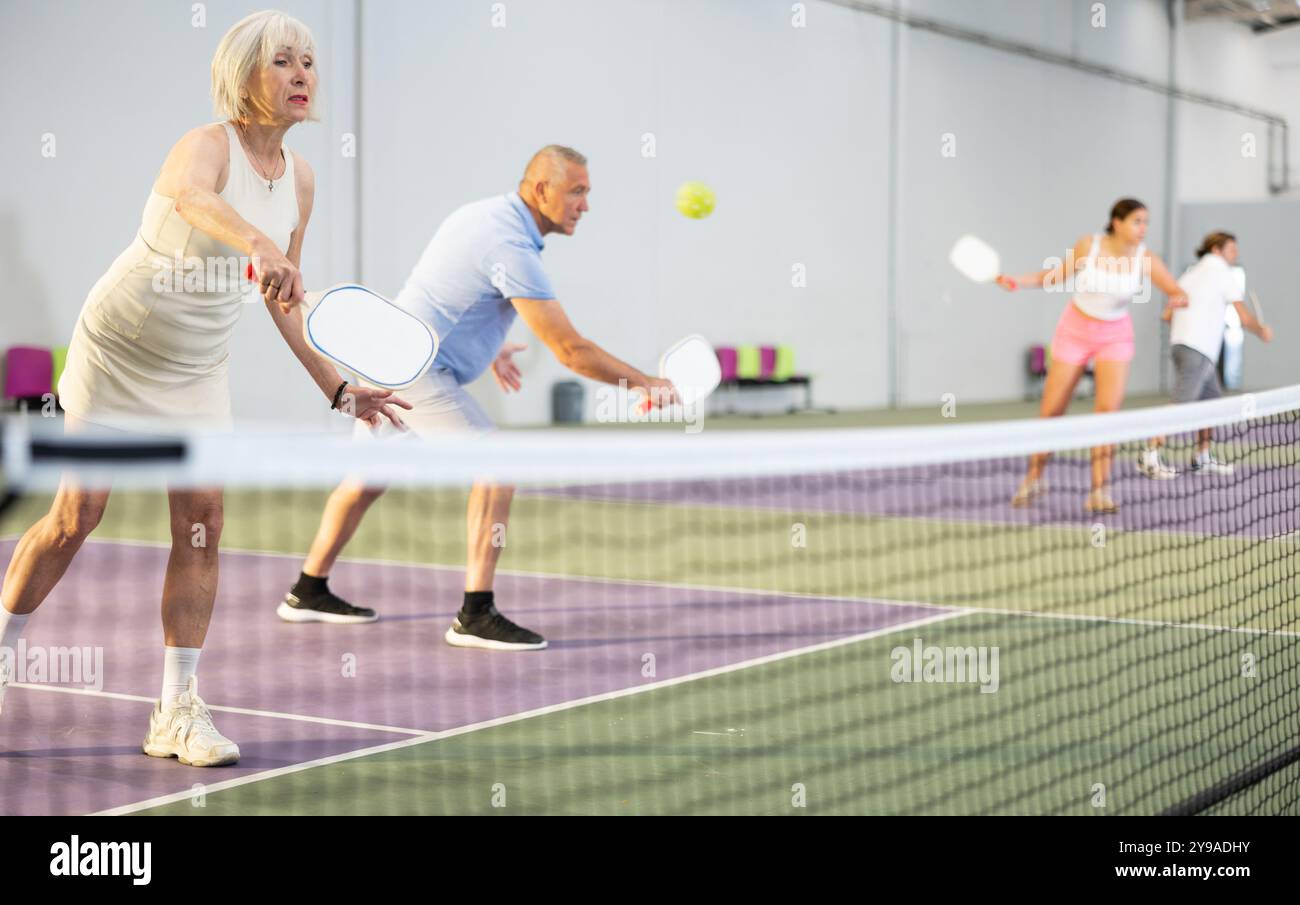 Senior woman playing doubles pickleball with male partner indoors Stock ...