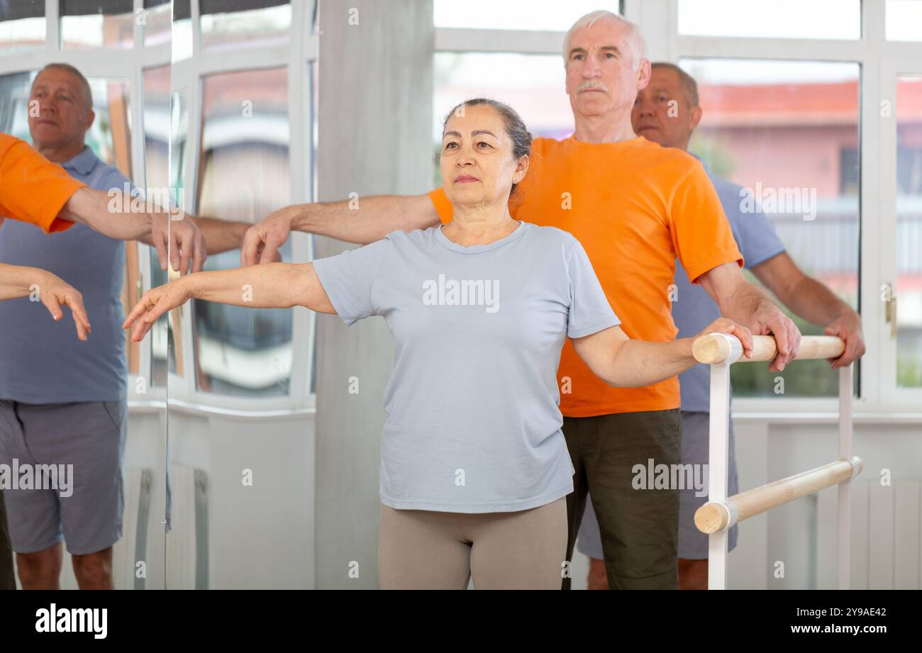 Pensioners of different ages exercise near ballet barre at group ...
