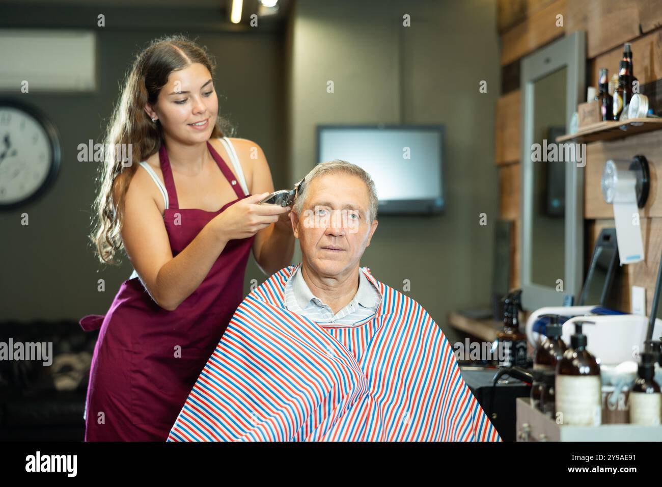 Young female barber making haircut to elderly client in barbershop ...