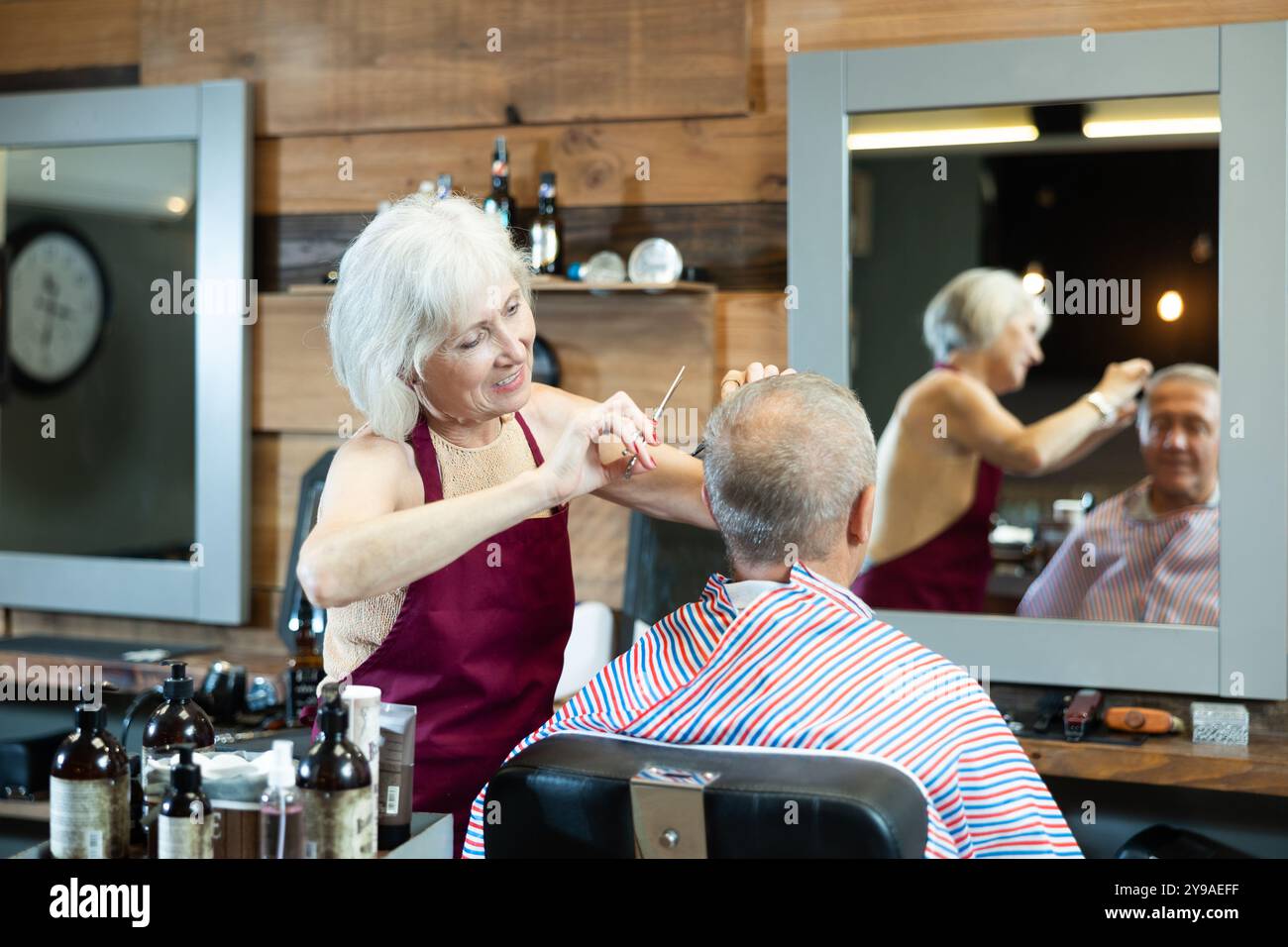 Female barber using scissors for haircut to gray-haired client in ...