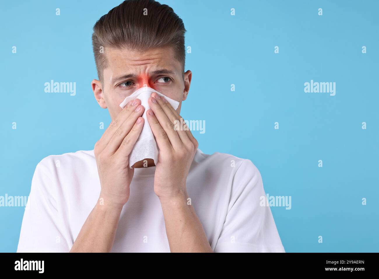 Young man with tissue suffering from sinusitis on light blue background ...