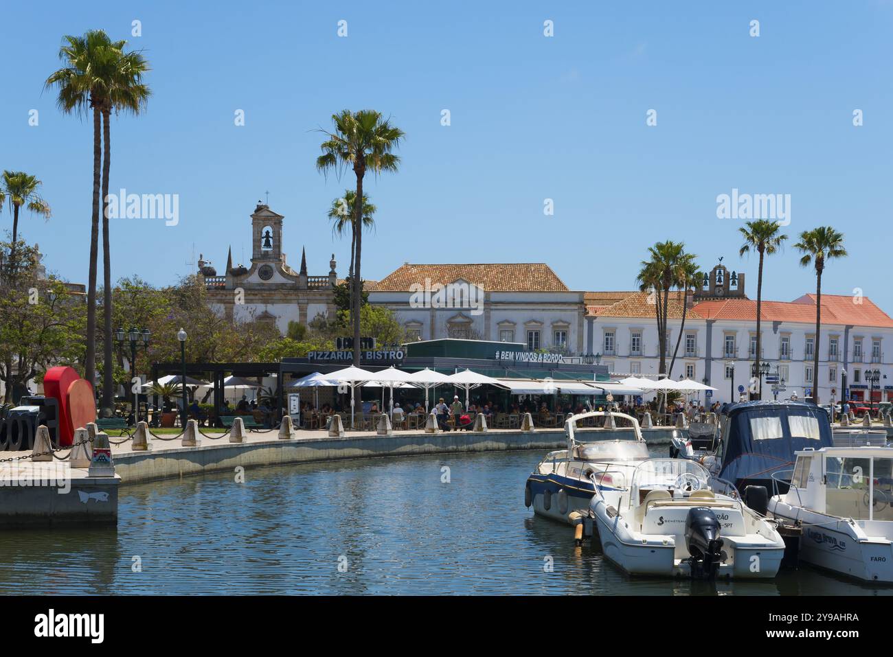 An idyllic harbour with boats and palm trees next to historic buildings ...