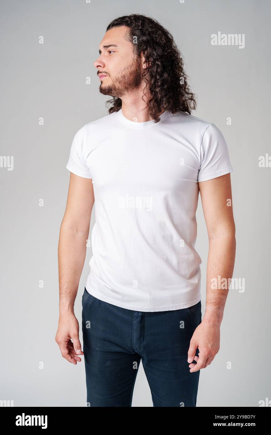 A young man stands confidently in profile, wearing a plain white t ...