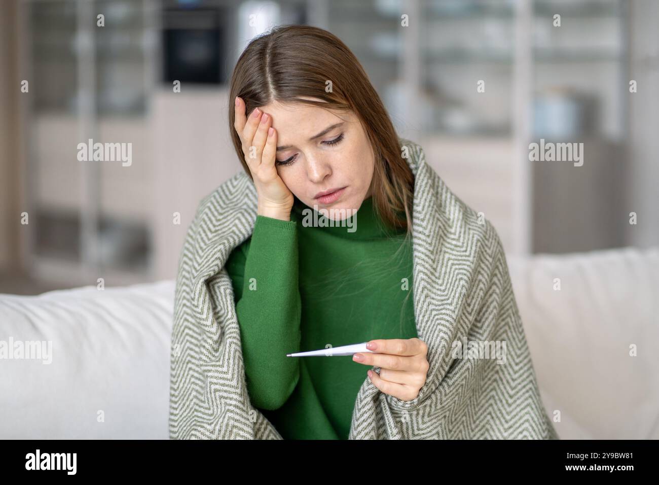 Sad sick woman measure temperature, holding head in hands on couch ...