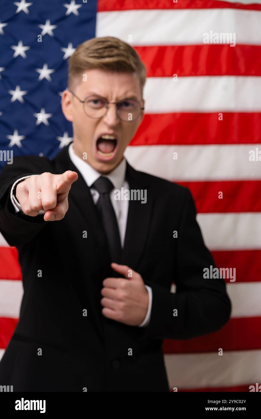 Man in a suit pointing at the American flag. He is wearing a tie and ...