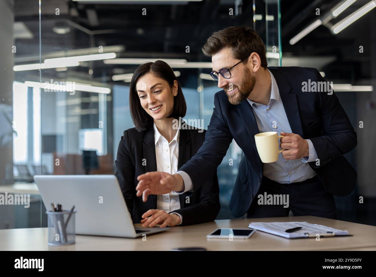 Colleagues in suits collaborating at work desk, focusing on laptop ...