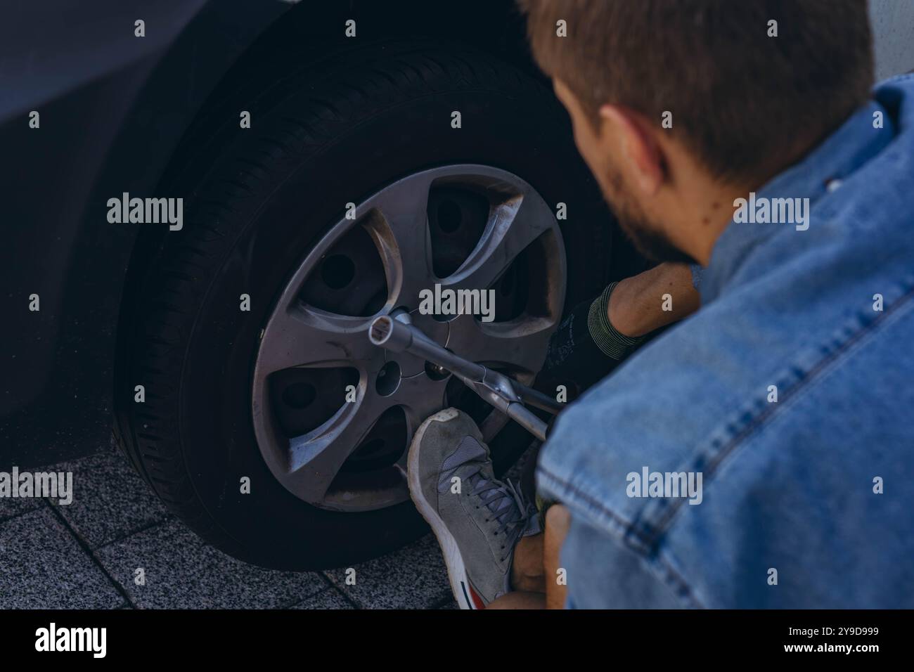 Young man in unscrewing lug nuts on car wheel in process of new tire ...
