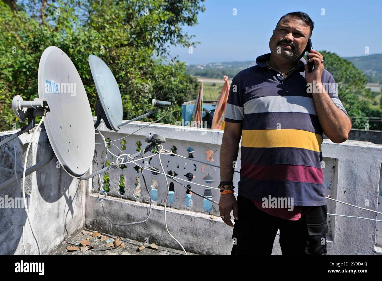A man talks on his mobile phone next to a Tata satellite dish at a slum ...