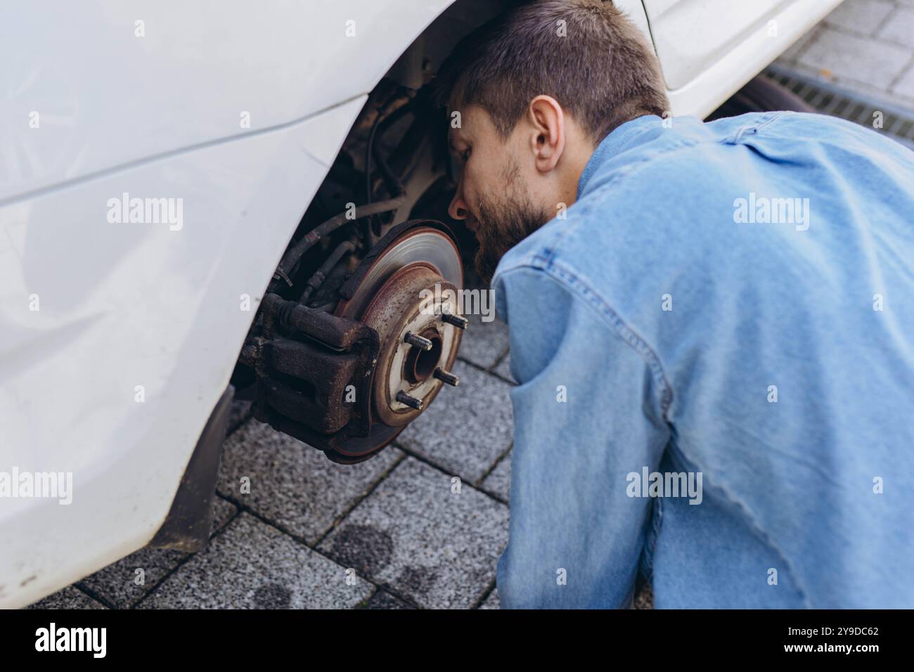 Young man in unscrewing lug nuts on car wheel in process of new tire ...