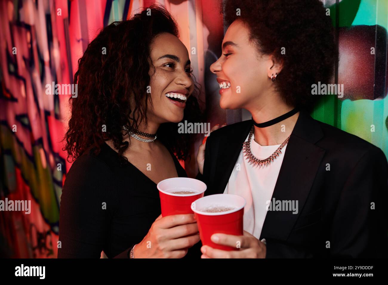 Friends share joyful moments and drinks against a colorful graffiti ...