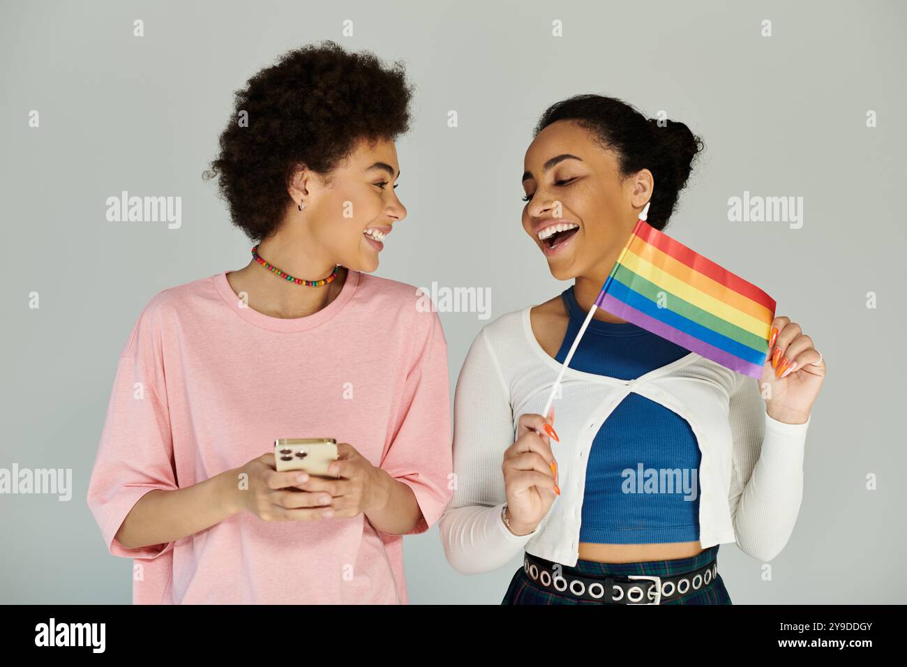 Two friends joyfully hold a rainbow flag, sharing laughter and each ...