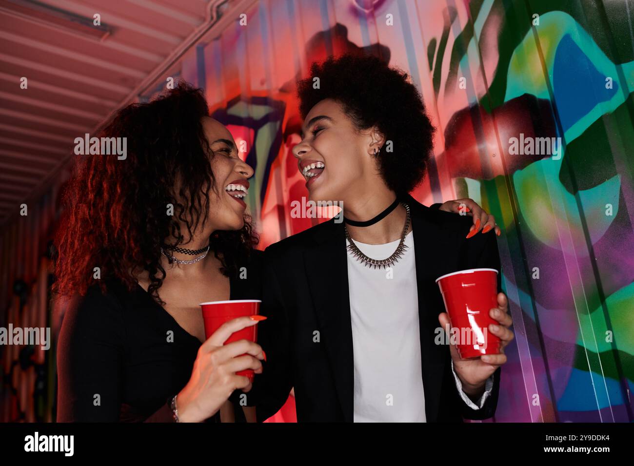 Two friends enjoy each others company, laughing while holding red cups ...