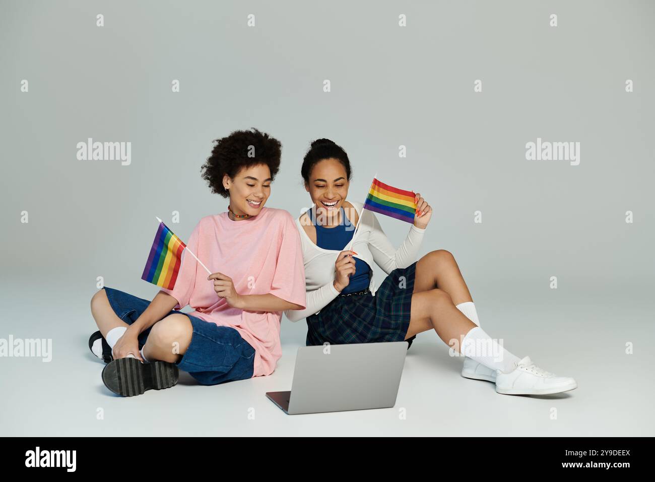 Two young women sit on the floor, waving rainbow flags and enjoying a ...