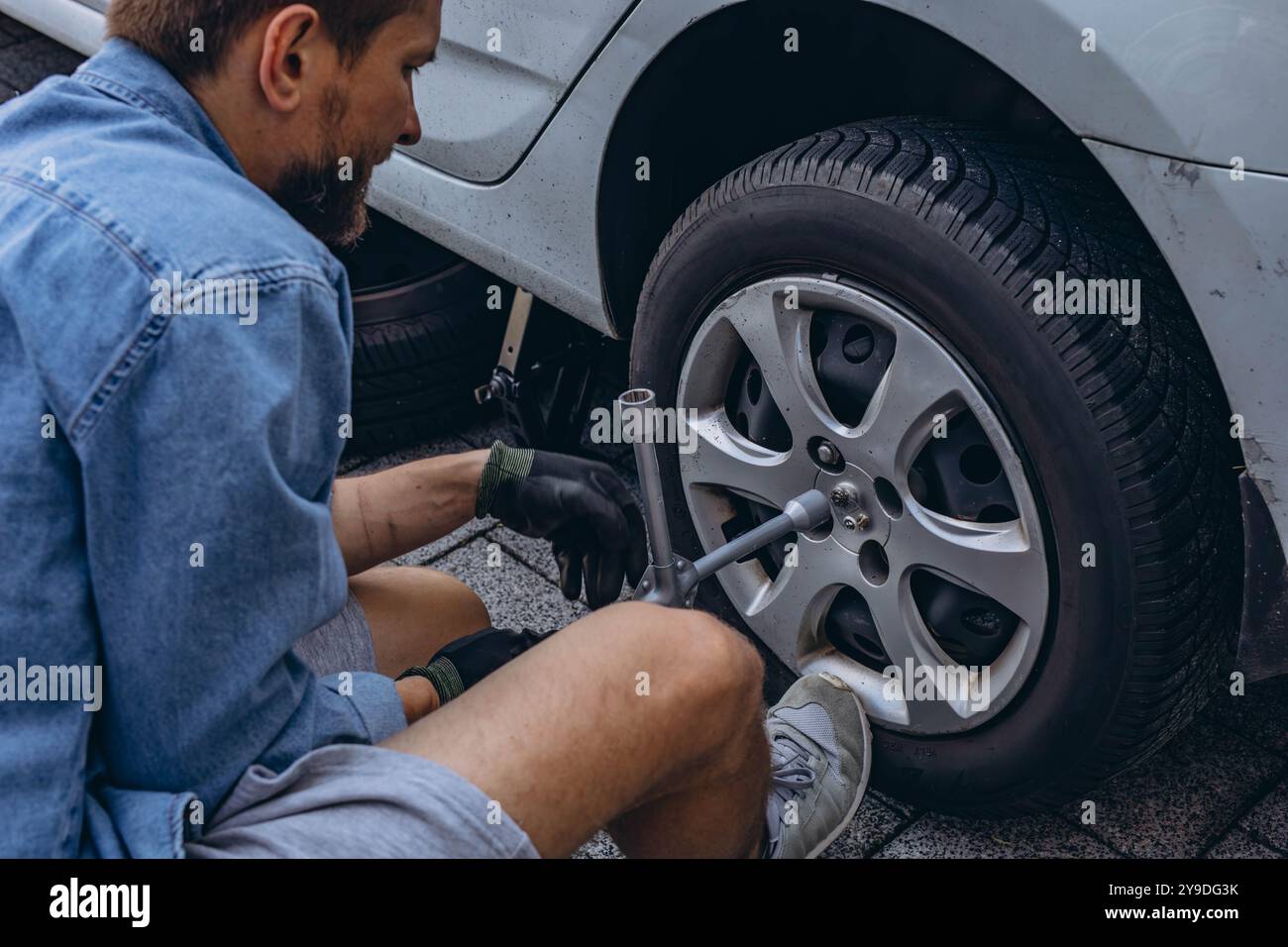 Young man in unscrewing lug nuts on car wheel in process of new tire ...