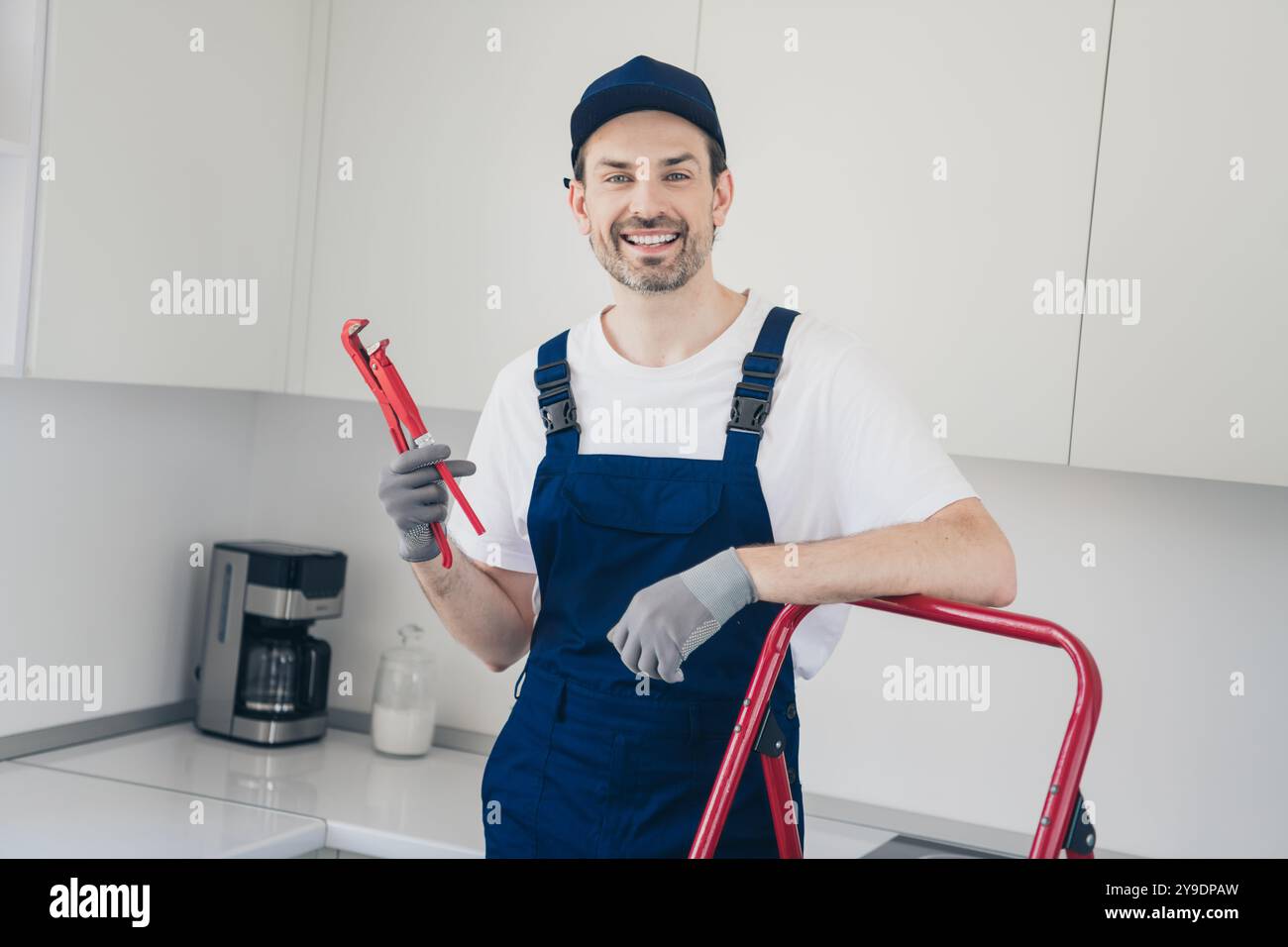 Smiling handyman standing with wrench in modern kitchen ready for ...