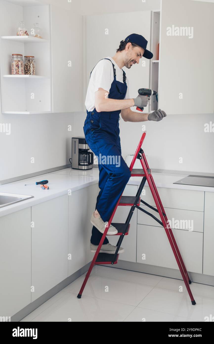Handyman on a ladder skillfully drilling into kitchen cabinet during ...