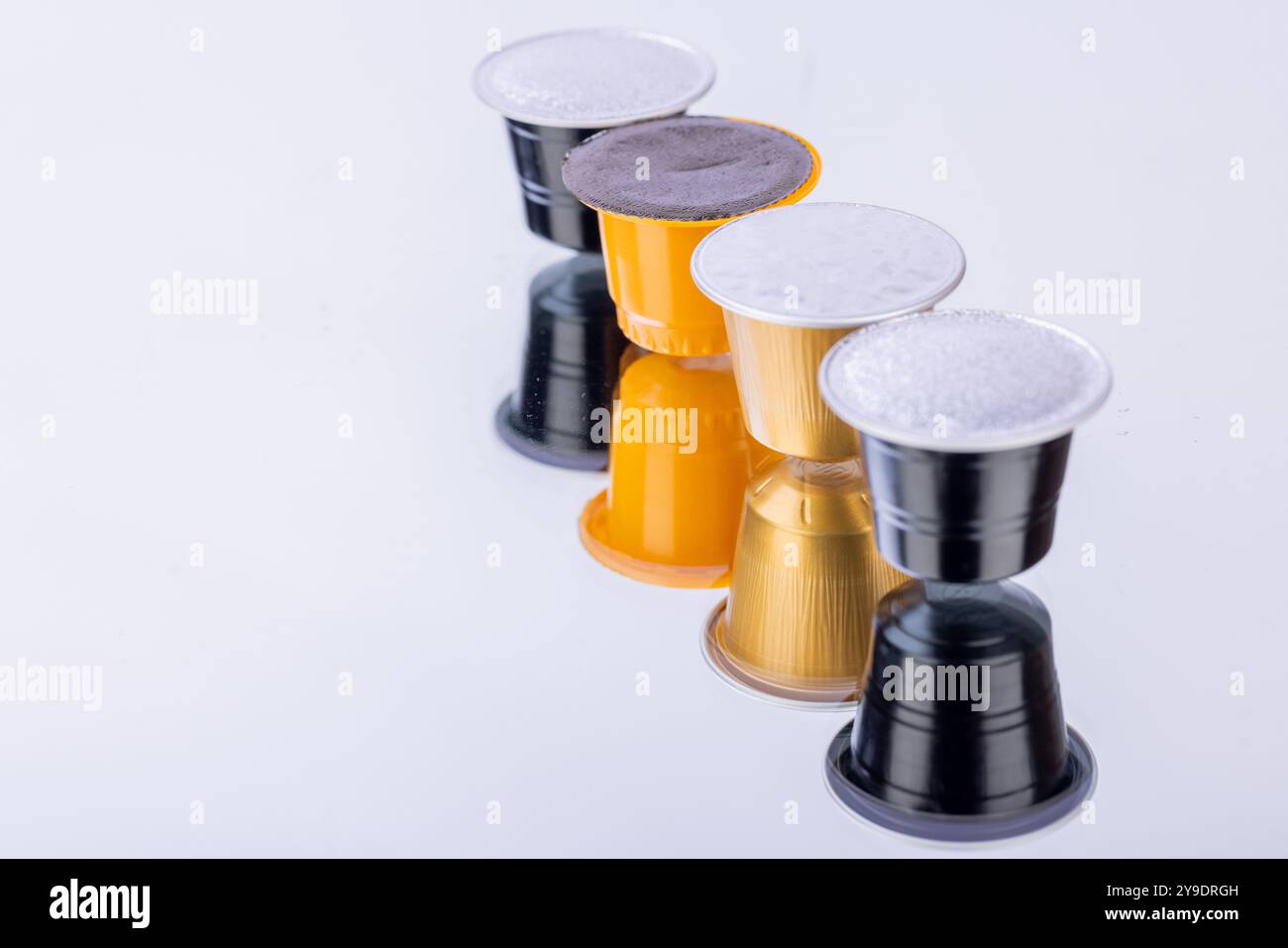 Assorted coffee capsules in vivid colors are set on a reflective mirror ...