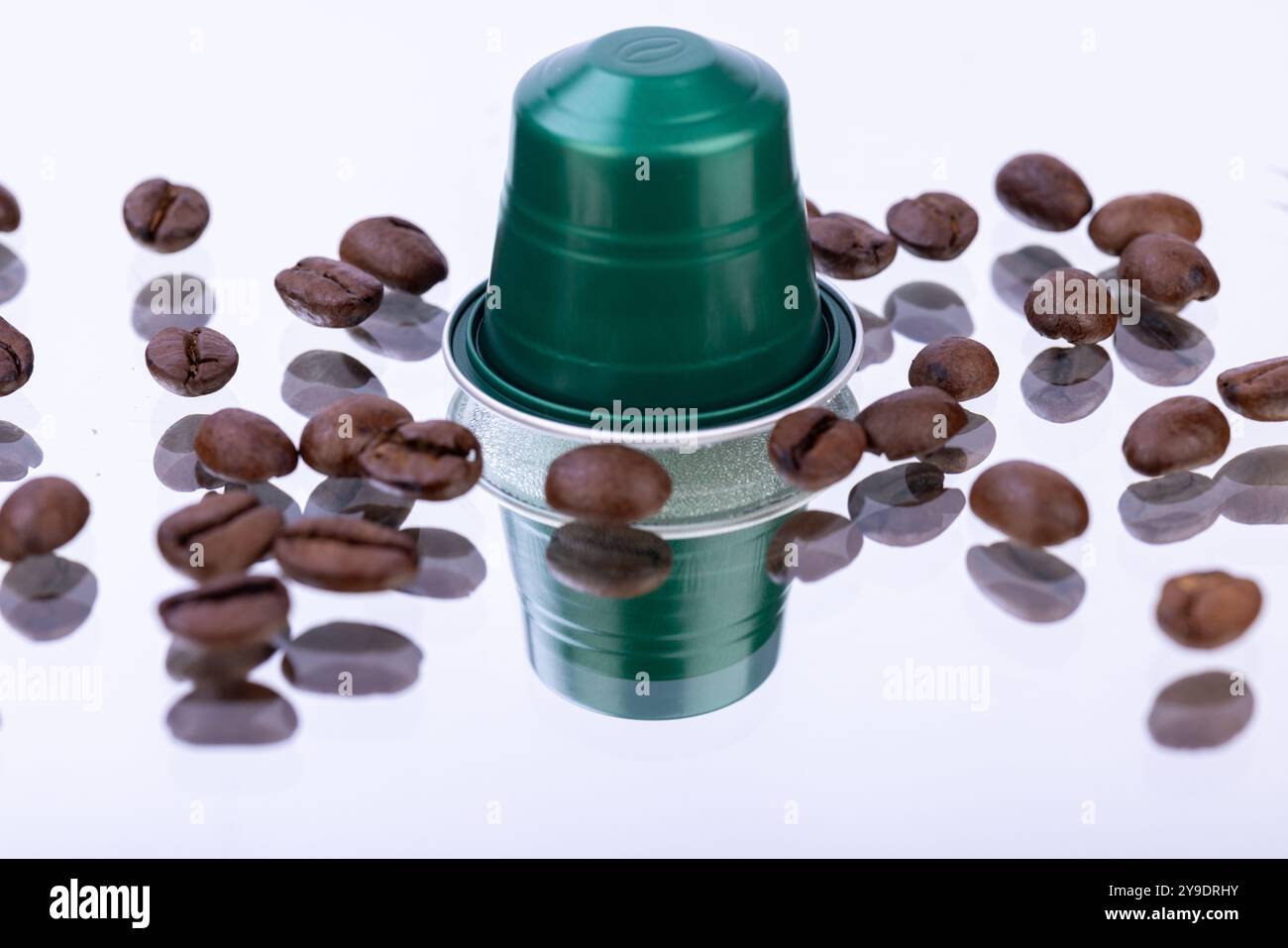Assorted coffee capsules and beans on a mirror, reflecting colors and ...