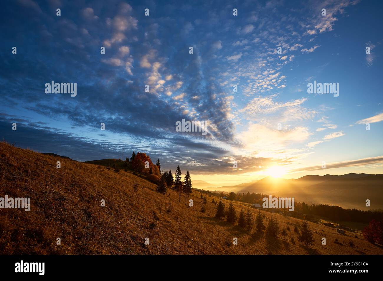 Sun rises over mountains, casting golden rays across landscape. Sky ...