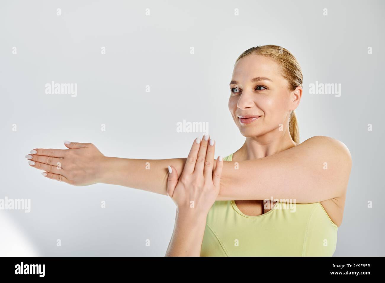 A dedicated woman in a crop top is stretching her arms in a bright ...