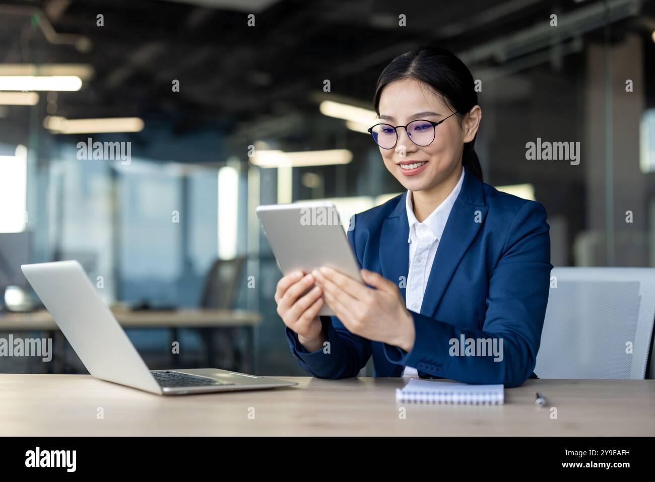 Asian business woman in office using tablet, wearing glasses and blue ...