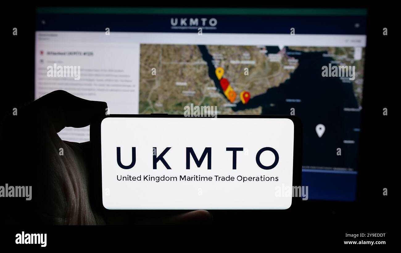 Person holding cellphone with logo of United Kingdom Maritime Trade ...
