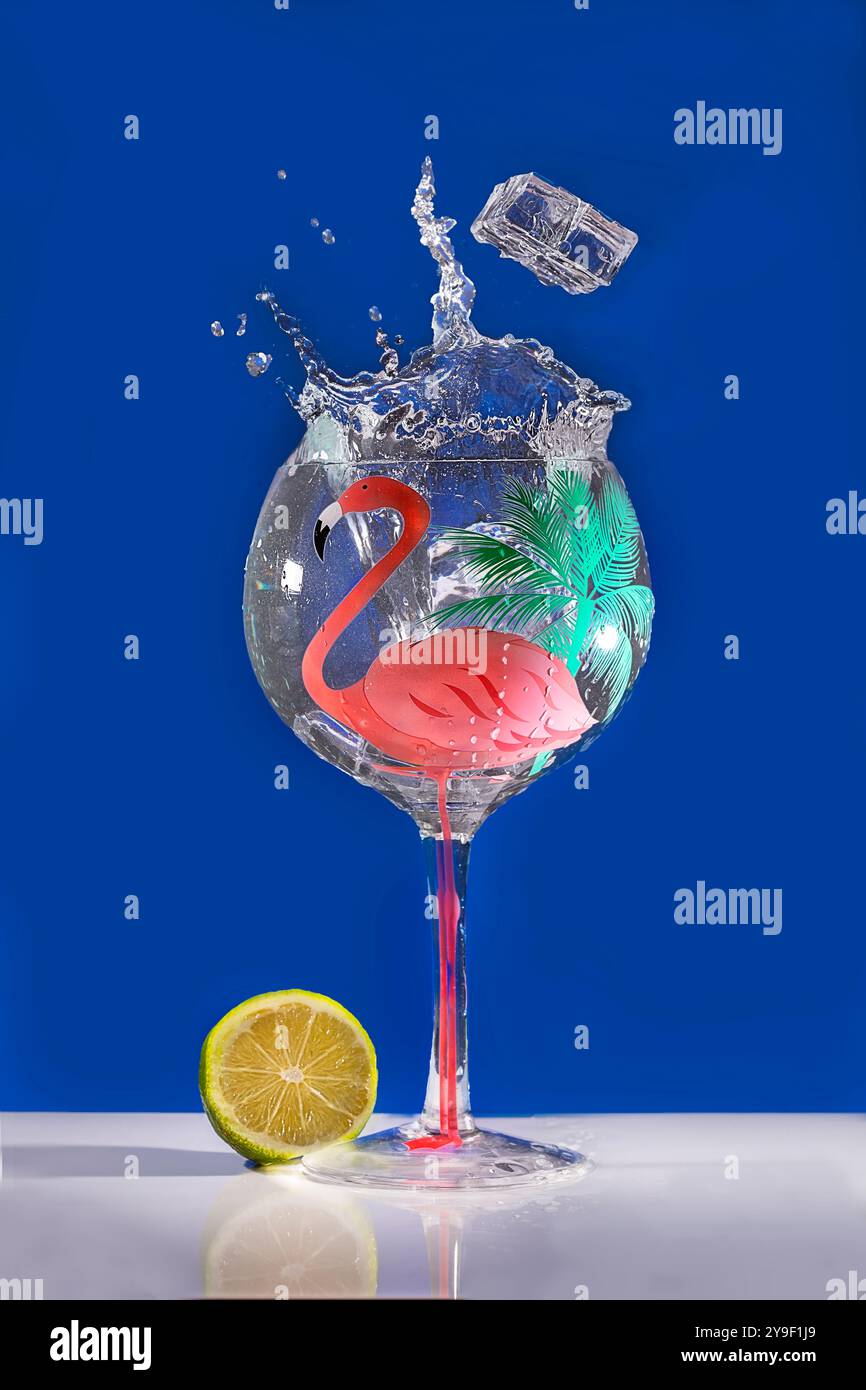 Flamingo decorated glass with gin and tonic and dropping ice cubes ...