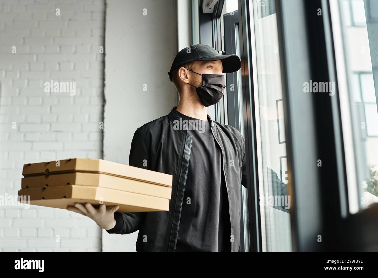 A delivery man wearing a black medical mask carries multiple food boxes ...