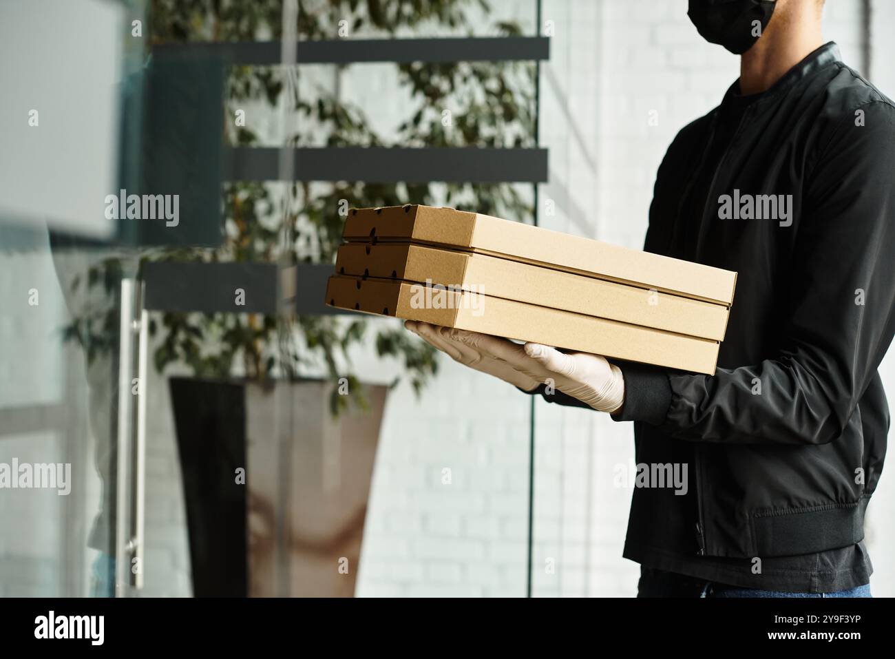 A delivery man wearing a black mask brings multiple pizza boxes into a ...