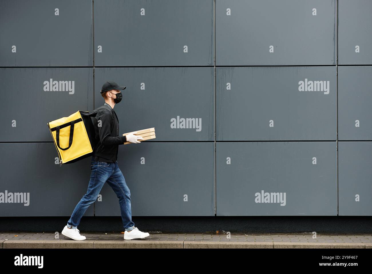 A delivery man in a black mask carries boxes into an office building ...