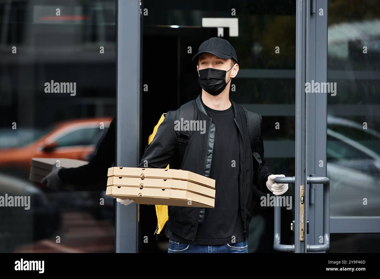 A delivery man in a black mask brings pizza boxes into a bustling ...