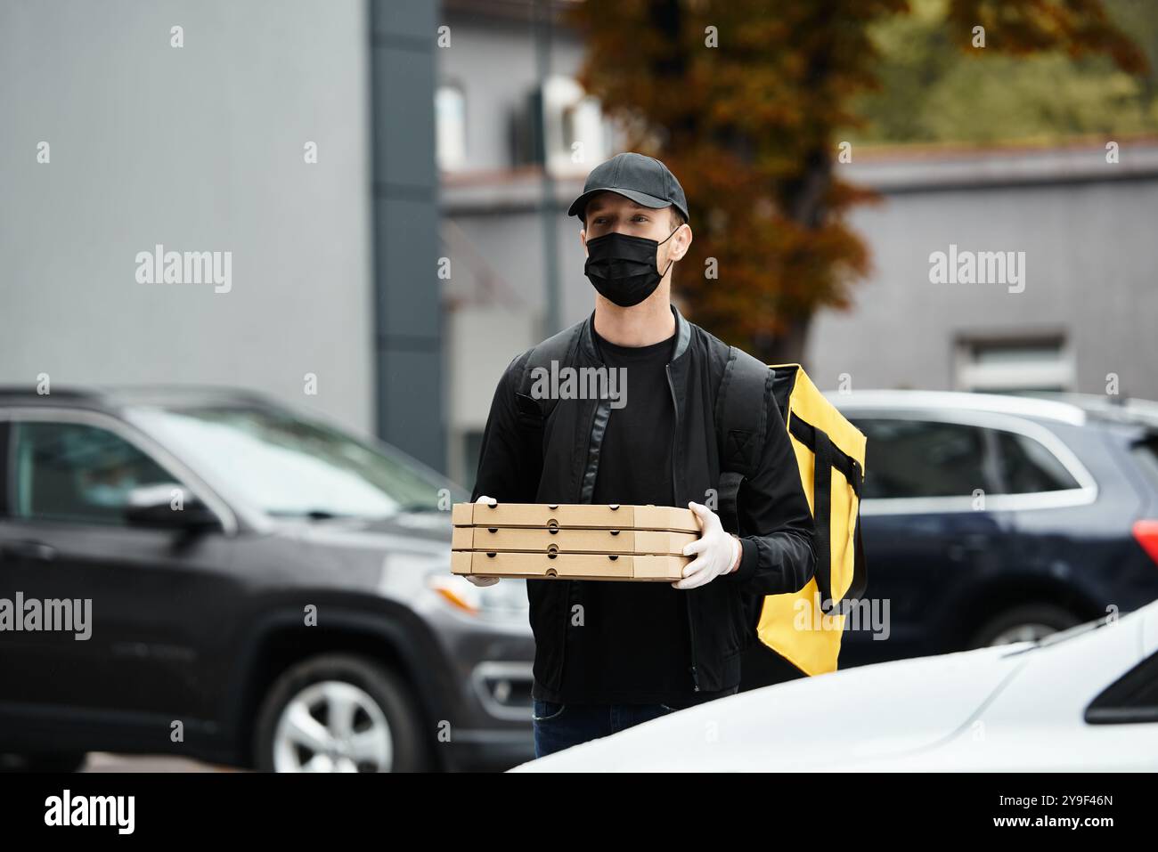 A delivery man in a black mask brings food orders into an office ...