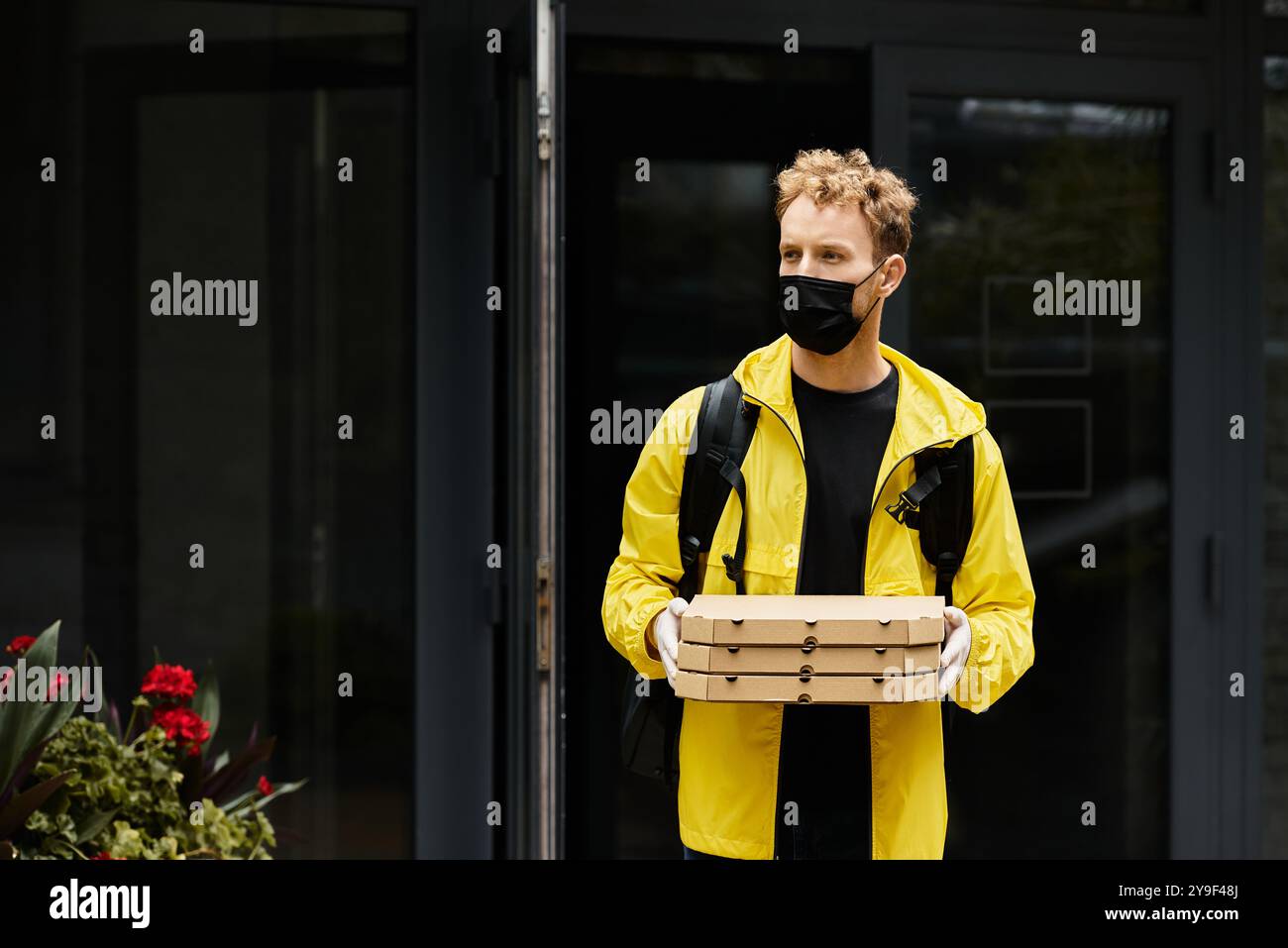 A delivery person wearing a black medical mask carries multiple pizza ...
