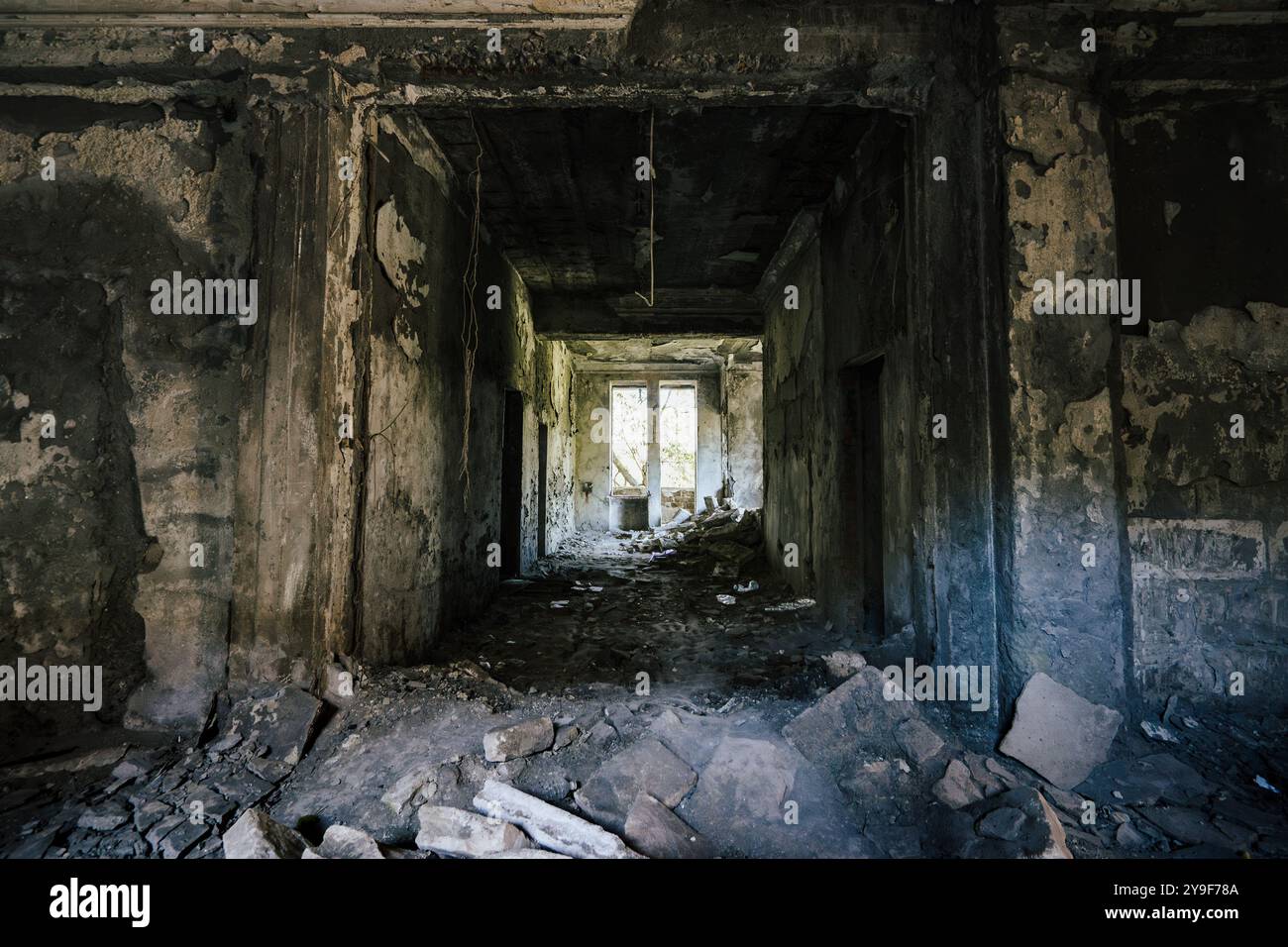 Abandoned corridor in dilapidated building with crumbling walls and debris scattered across the ...