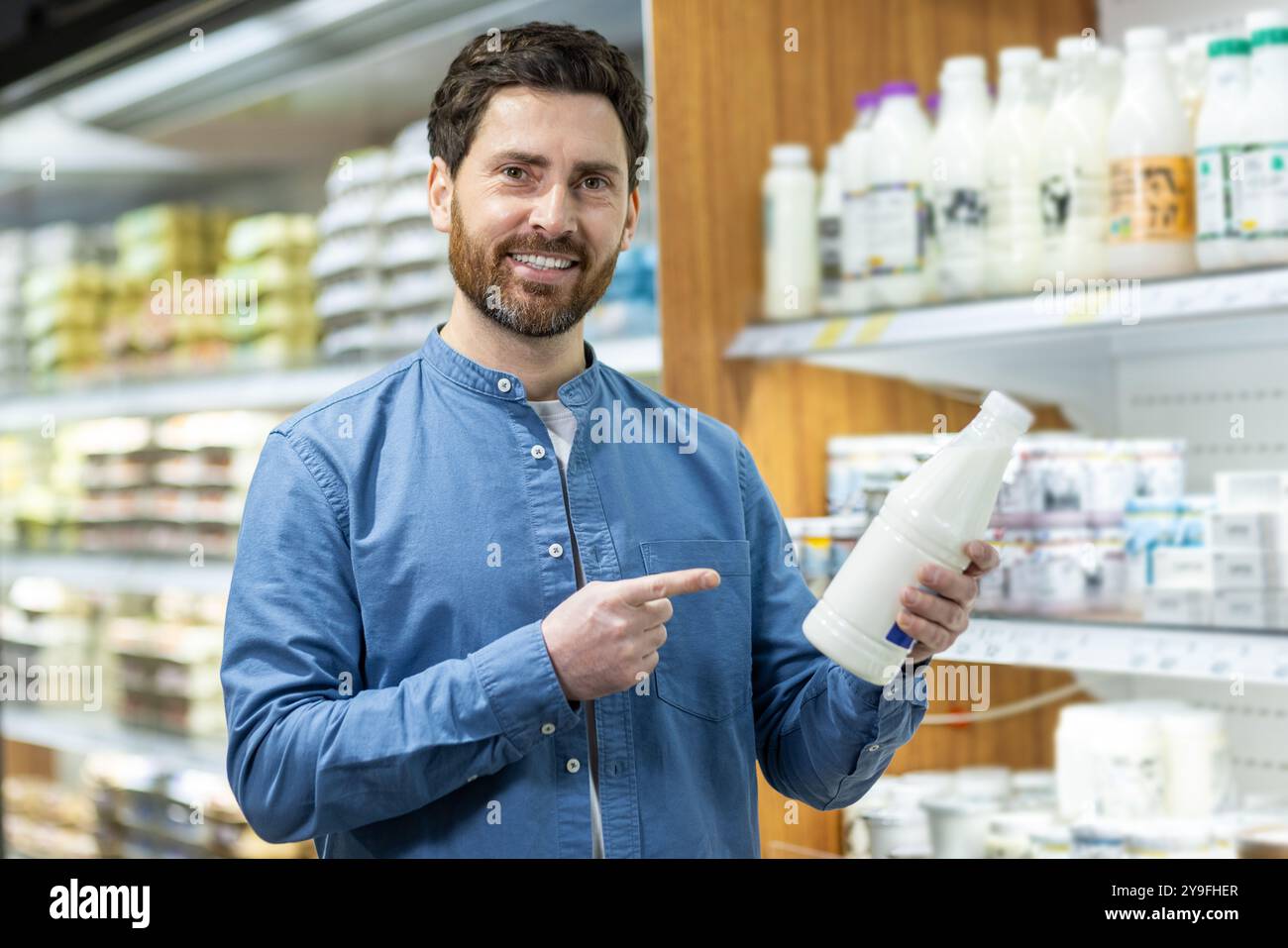 Smiling man in supermarket pointing at milk bottle in refrigerated ...