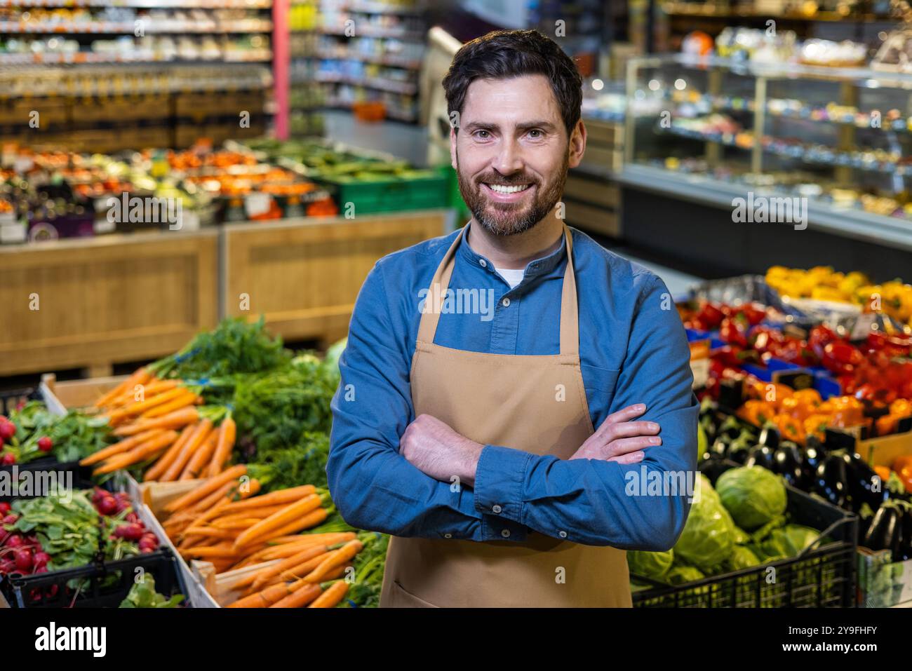 Grocery store worker in apron confidently poses in produce section ...
