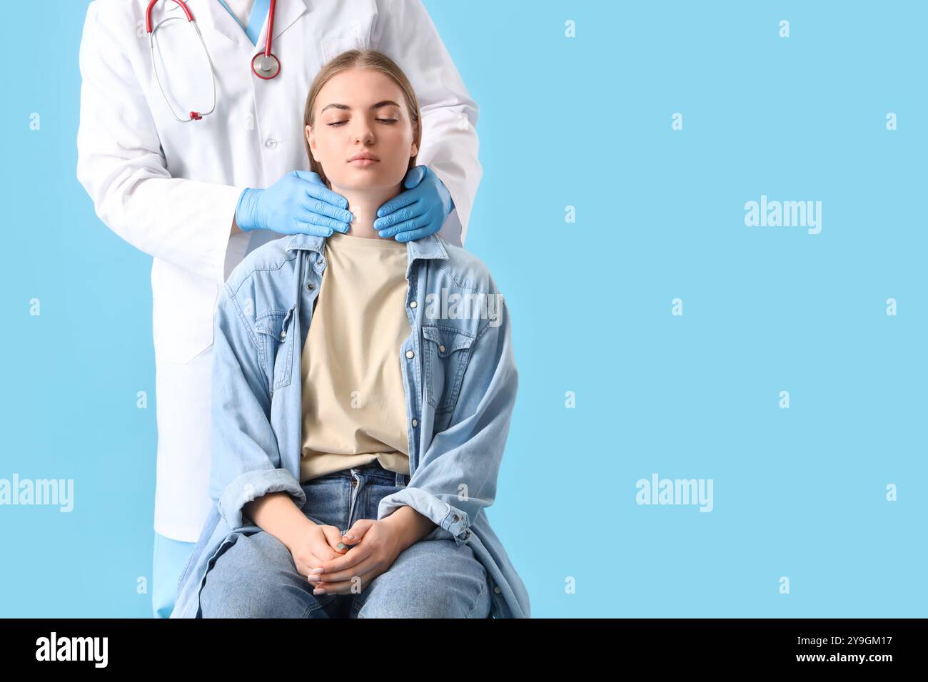 Male endocrinologist examining woman's thyroid gland on blue background ...
