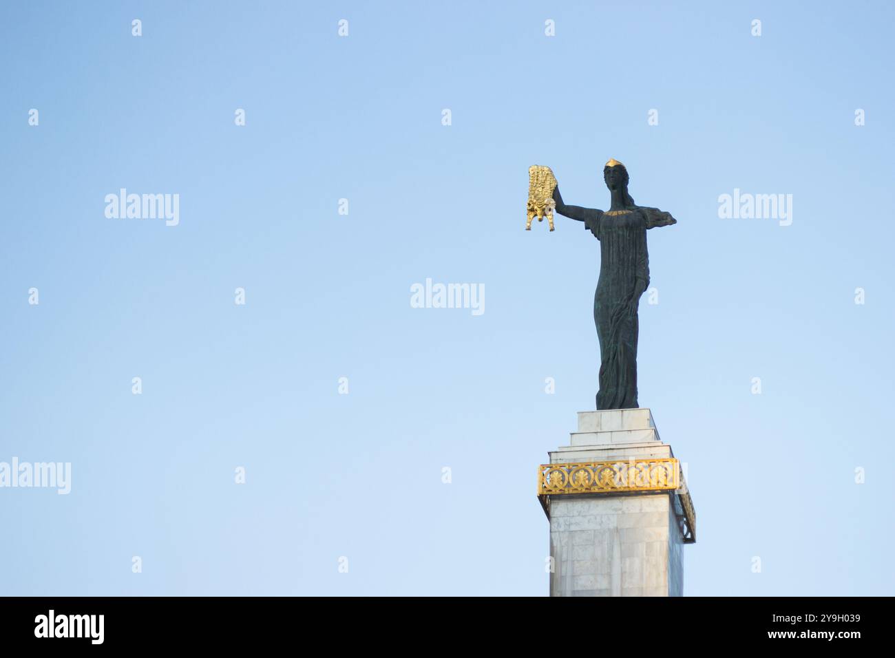 a striking statue atop a tall pedestal, holding a golden fleece high in ...