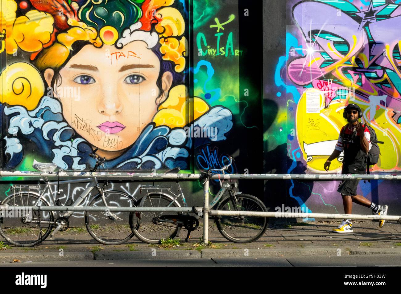 A man with headphones walks along a colorful wall Street Art Berlin ...